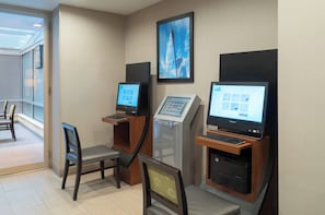 Um saguão de hotel com balcão de recepção, uma cadeira, um computador e uma impressora.