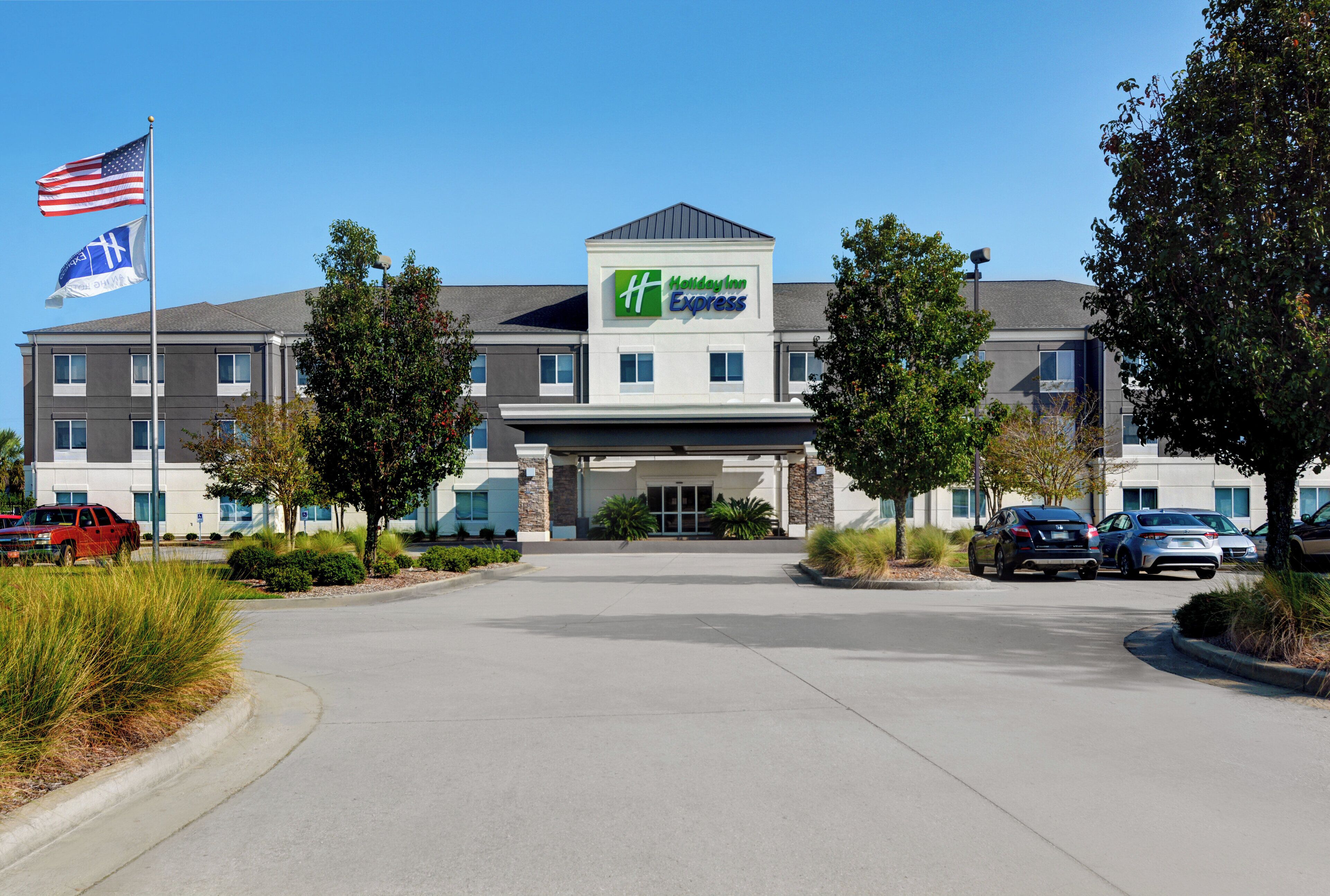 Um hotel Holiday Inn Express com entrada visível, área de estacionamento e exibição de bandeiras.