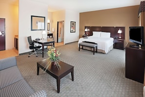 Quarto de hotel com cama, escrivaninha, cadeira, televisão e sofá.
