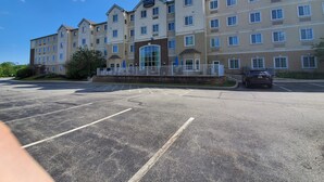 Um hotel com vários andares, entrada central, estacionamento e céu azul claro.