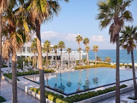 Um resort com piscina, palmeiras e vista para o oceano.