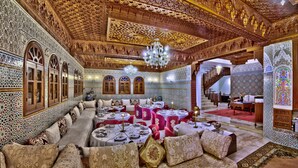 Uma sala de jantar luxuosa com trabalhos em azulejos requintados, um candelabro e uma escadaria para um andar superior.