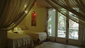 Quarto com duas camas, dossel, mesa de cabeceira, luminária na parede e uma grande janela com vista para o exterior.