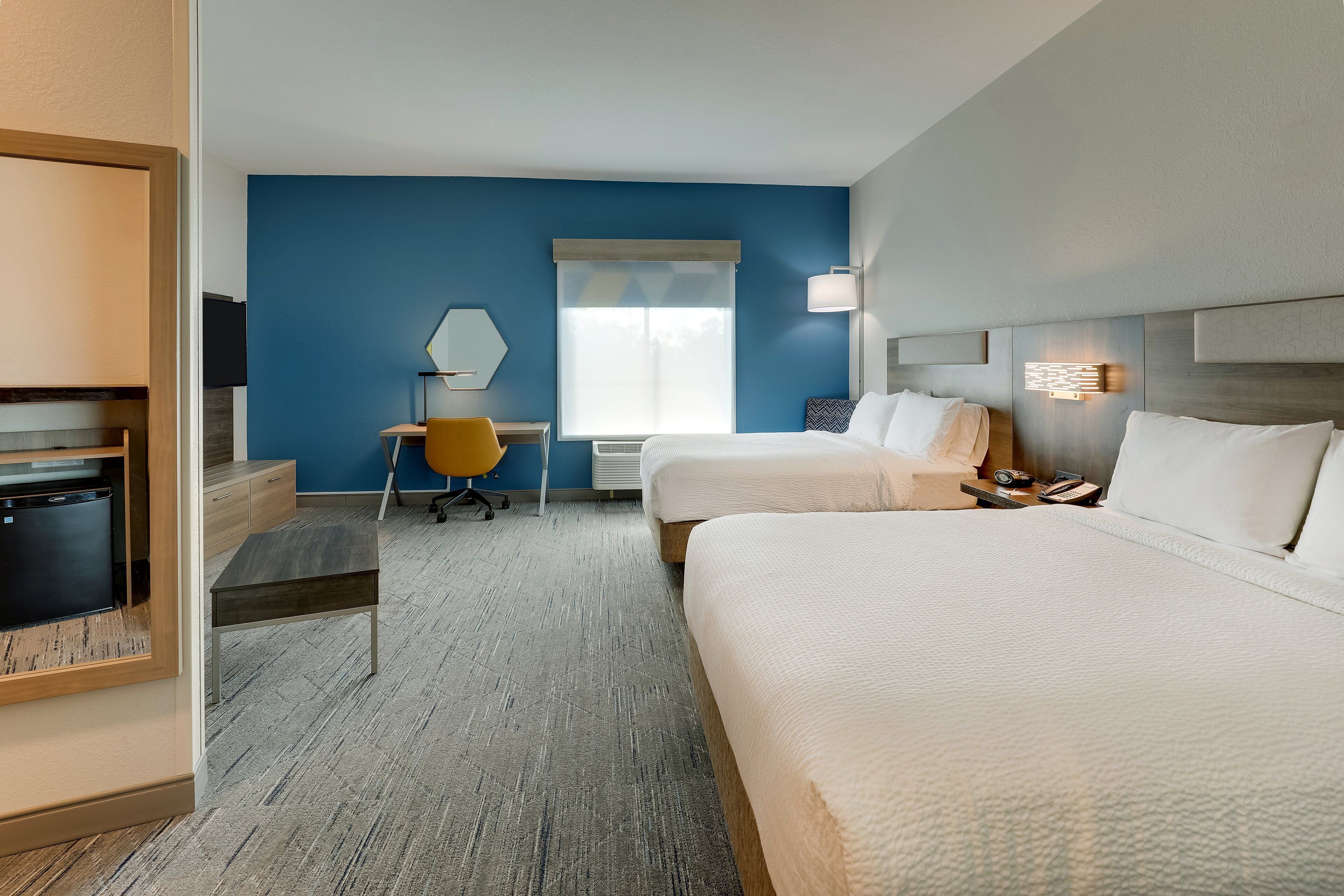 Quarto de hotel com duas camas, uma mesa, uma cadeira, uma televisão e uma janela com cortinas.