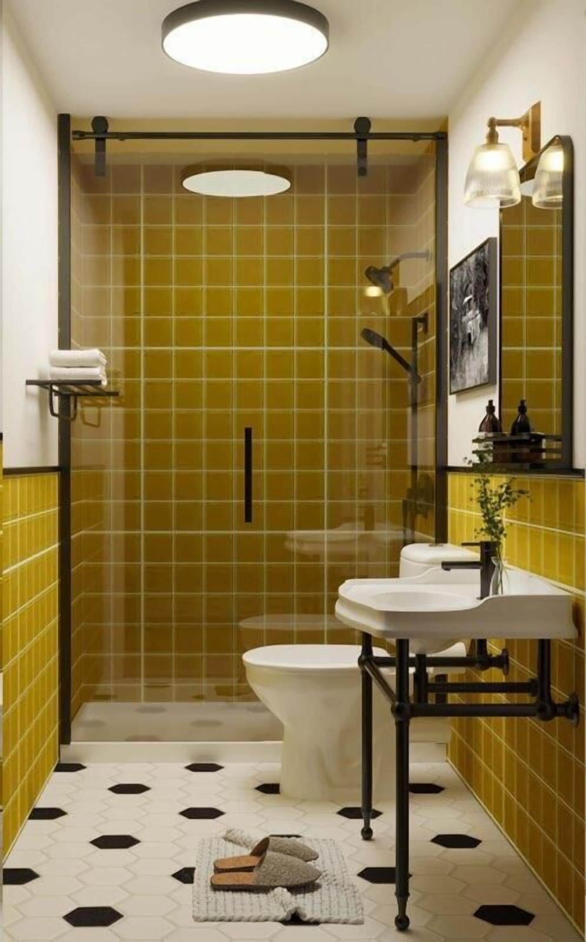 Casa de banho com paredes azulejadas amarelas, sanita branca, lavatório com estrutura preta, espelho e zona de duche.