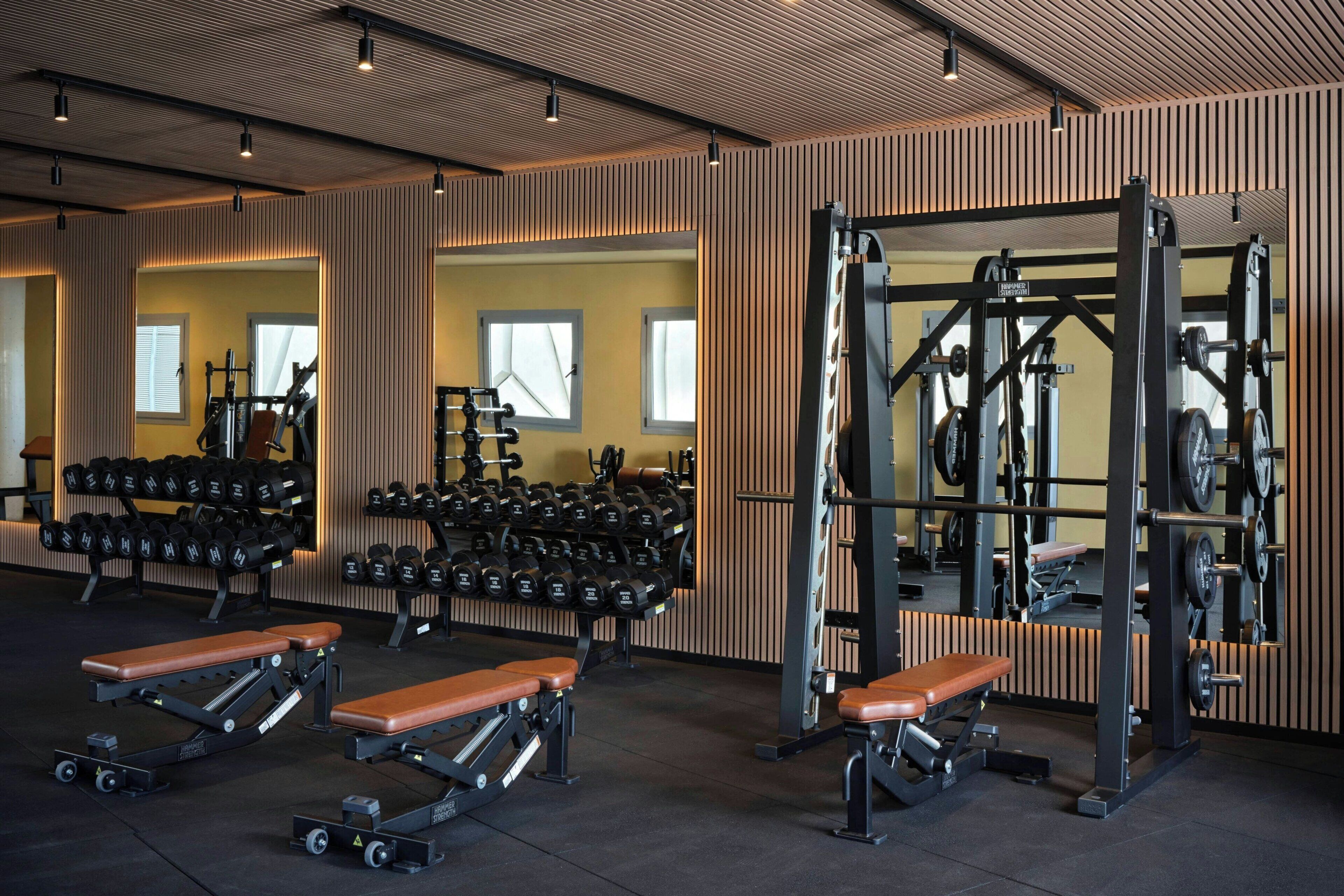 Uma academia com equipamentos de musculação, bancos e halteres.