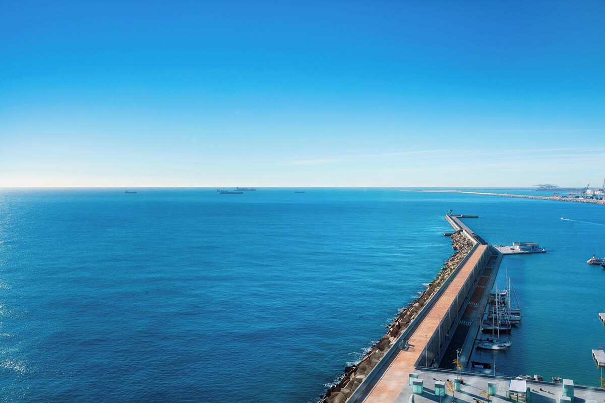 Um porto costeiro com um cais longo que se estende até o mar, vários barcos atracados e um céu limpo.