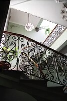 Escadaria com grades de metal preto ricamente decoradas e parede branca com desenho floral.
