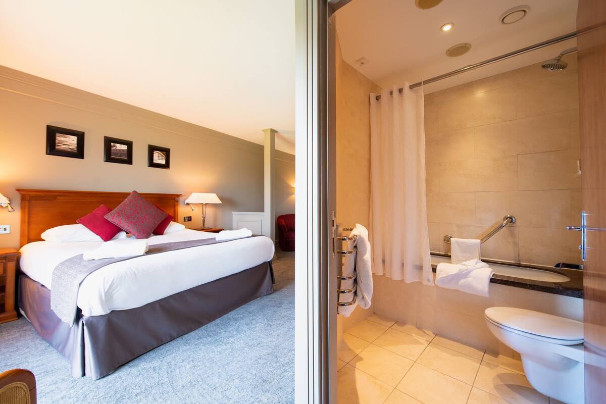 Quarto de hotel com cama, mesas de cabeceira, casa de banho com chuveiro, sanita e lavatório.
