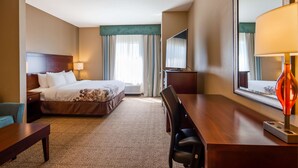Quarto de hotel com cama, escrivaninha, cadeira, luminária, televisão e janela com cortinas.