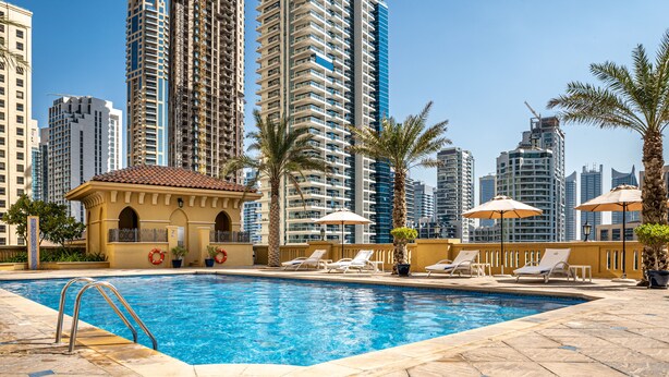 Piscina com espreguiçadeiras e guarda-sóis, rodeada por edifícios altos.