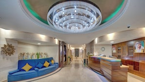 Um hall de hotel com um sofá azul, um balcão de recepção e um grande lustre.