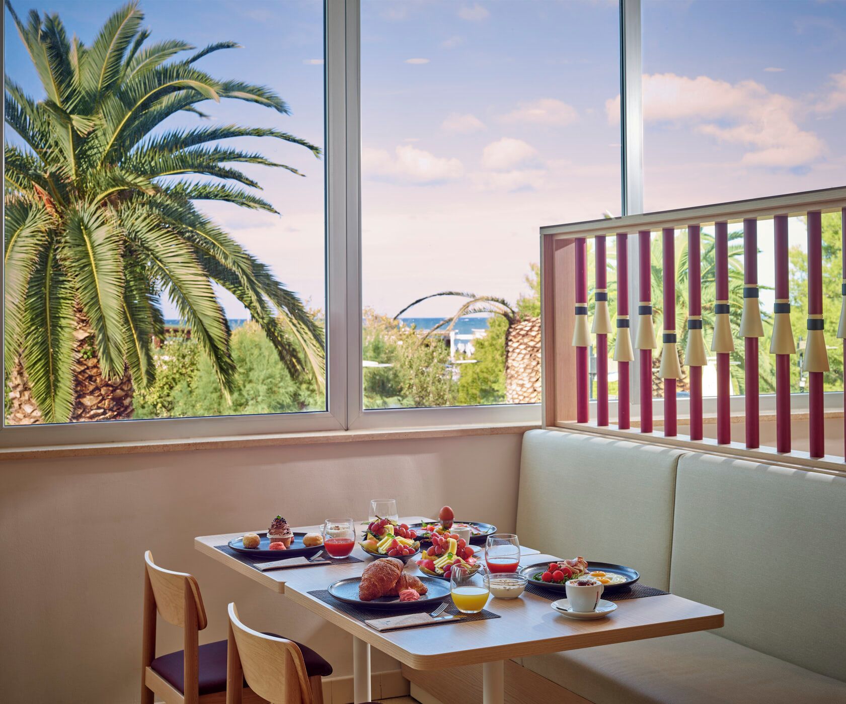 Uma área de refeições com uma mesa posta para o café da manhã, com vista para uma palmeira e o mar.