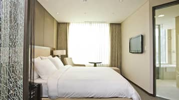 Quarto de hotel com uma cama grande, uma mesa, uma cadeira, uma TV e uma porta de vidro que dá para um banheiro.