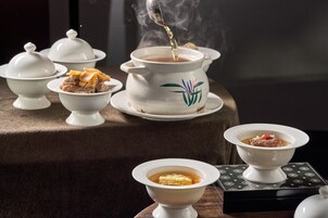 Uma mesa com uma chaleira branca, uma tigela de sopa e um prato de comida.