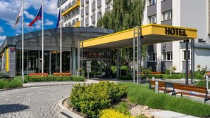 Entrada de hotel com galeria coberta, bandeiras e céu limpo.