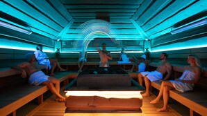 Uma sauna com bancos de madeira, chão aquecido central e iluminação azul no teto.