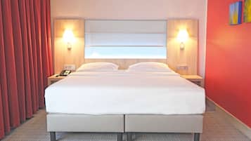 Uma cama de casal com cabeceira, duas mesas de cabeceira com abajures, um telefone e uma cortina vermelha.