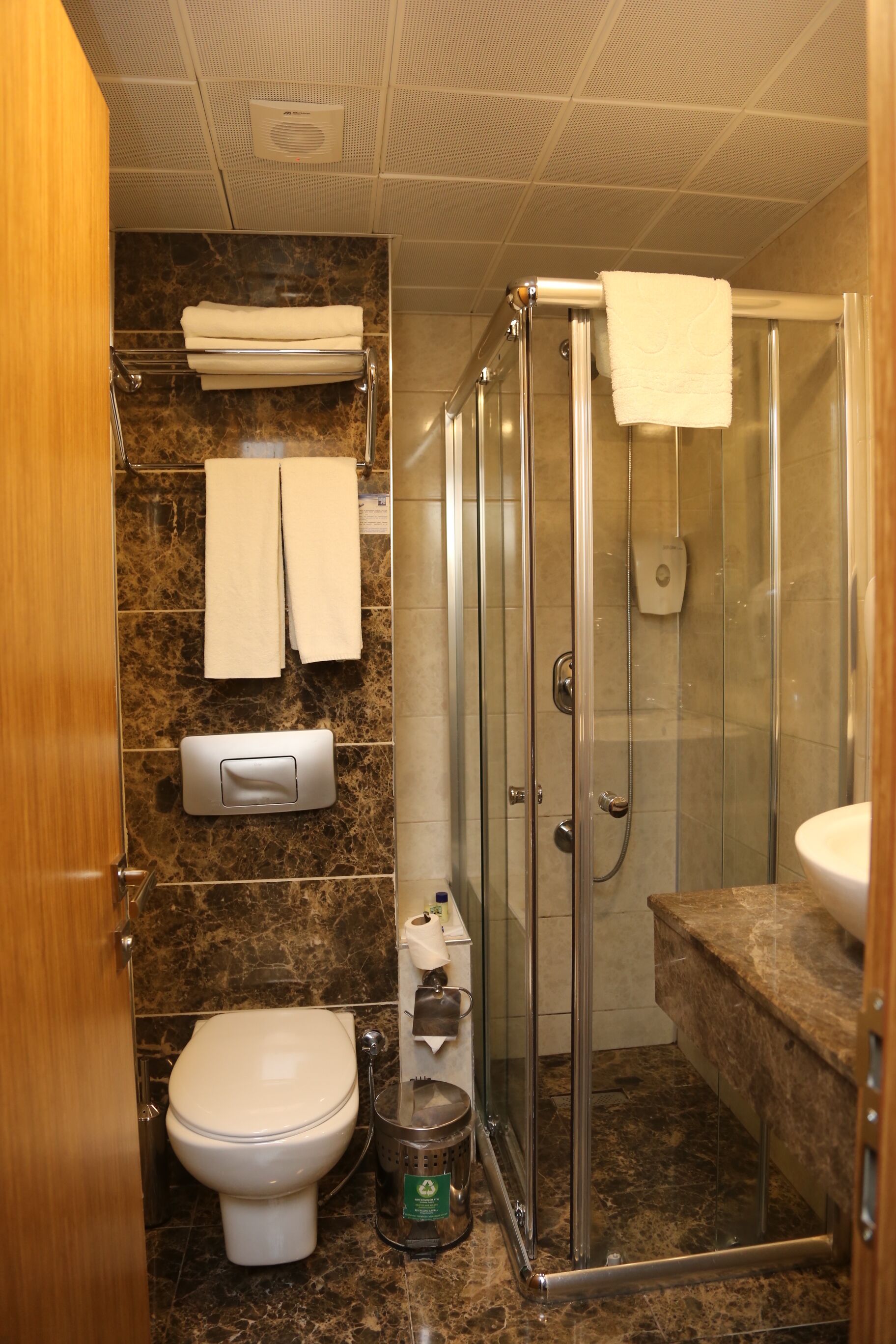 Casa de banho com sanita, cabine de duche em vidro, lavatório e suporte de toalhas com toalhas.