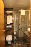 Casa de banho com sanita, cabine de duche em vidro, lavatório e suporte de toalhas com toalhas.