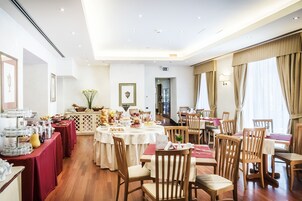 Uma sala de jantar com mesas redondas, cadeiras de madeira e um buffet com diversos tipos de comida.