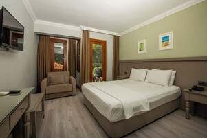 Quarto de hotel com cama, televisão, escrivaninha, cadeira e janela com cortinas.