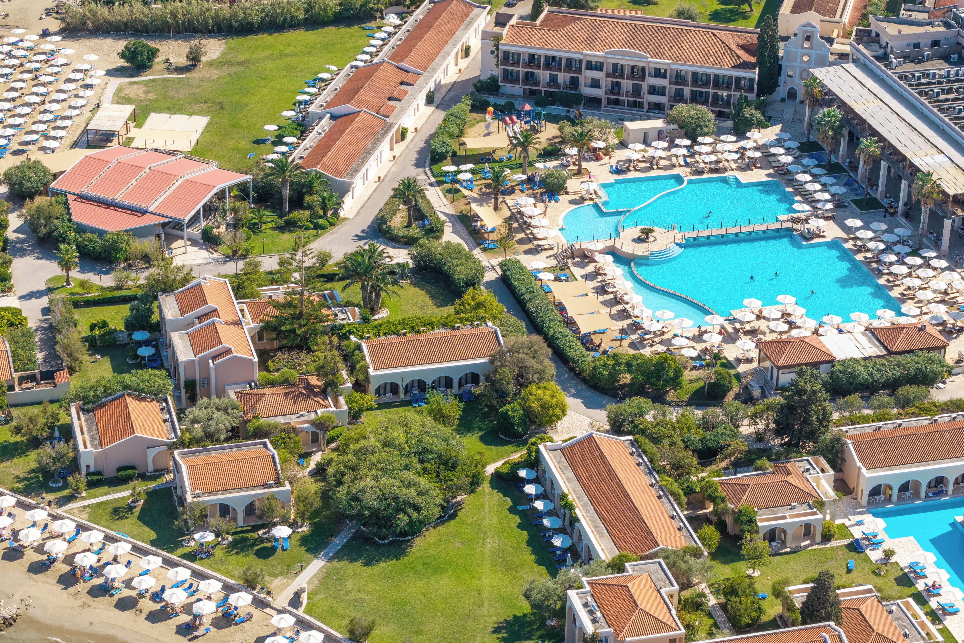Vista aérea de um resort com várias piscinas, espreguiçadeiras e um jardim bem cuidado.