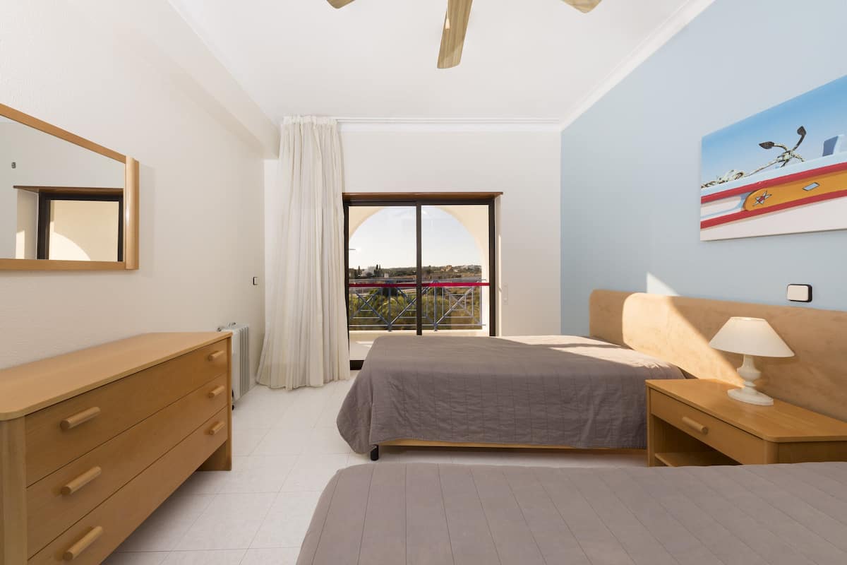 Quarto com cama, mesa de cabeceira, cômoda, janela com vista e ventilador de teto.
