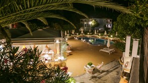 Vista noturna de um resort com piscina, espreguiçadeiras e guarda-sóis.