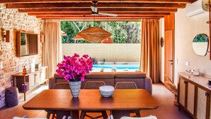 Uma área de refeições com uma mesa de madeira e cadeiras de vime, um sofá e um vaso com flores cor-de-rosa.