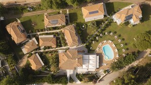 Vista aérea de um resort com vários edifícios, piscina e vegetação ao redor.