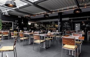 Um restaurante com várias mesas e cadeiras, um bar e uma cozinha ao fundo.