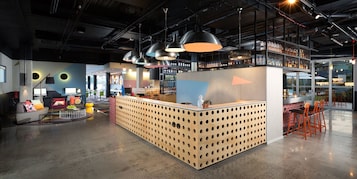 Uma área de bar moderna com balcão de madeira, iluminação pendente e vista para a cidade através de grandes janelas.
