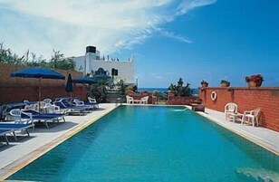 Piscina com espreguiçadeiras e guarda-sóis, uma parede de tijolos e um céu azul límpido.