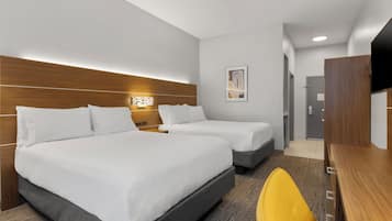 Quarto de hotel moderno com duas camas, cabeceira de madeira, uma cadeira amarela e televisão de tela plana.