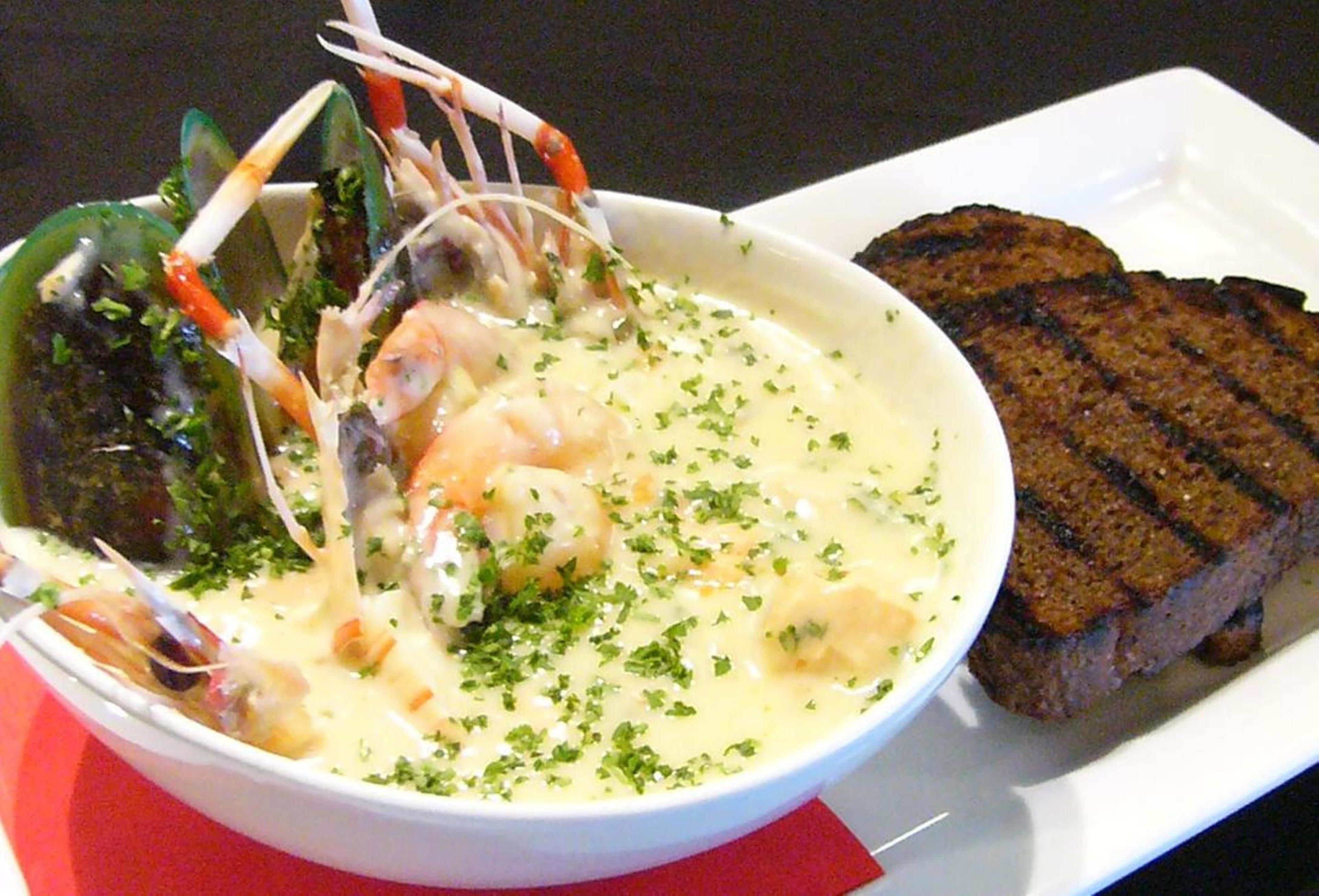Uma tigela de ensopado de frutos do mar com camarão e legumes, e um bife grelhado num prato branco.