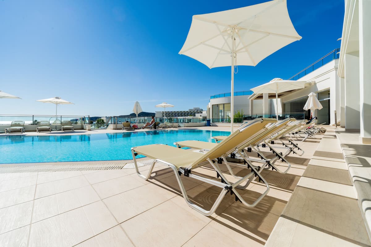 Área da piscina com espreguiçadeiras, guarda-sóis e um céu azul límpido.