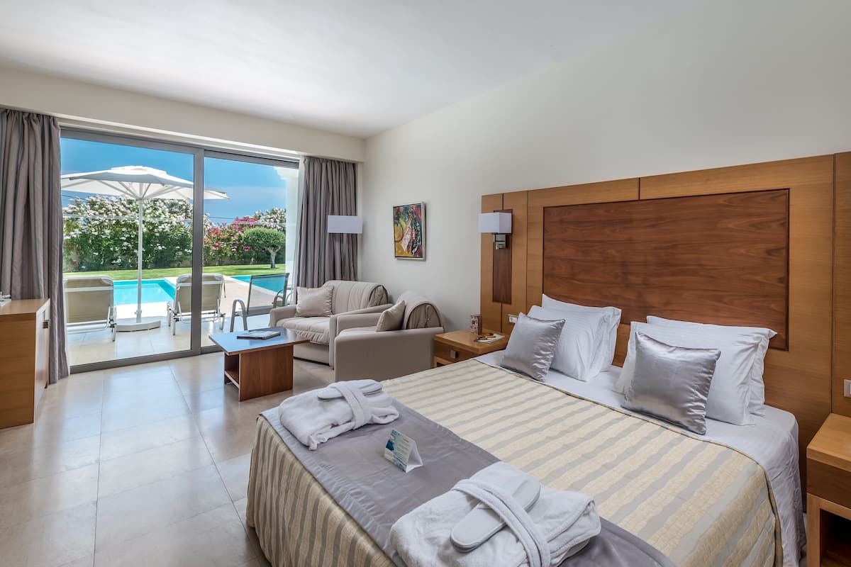 Quarto de hotel com uma cama grande, uma escrivaninha, uma cadeira, uma mesinha, vista para a piscina e cabeceira de madeira.