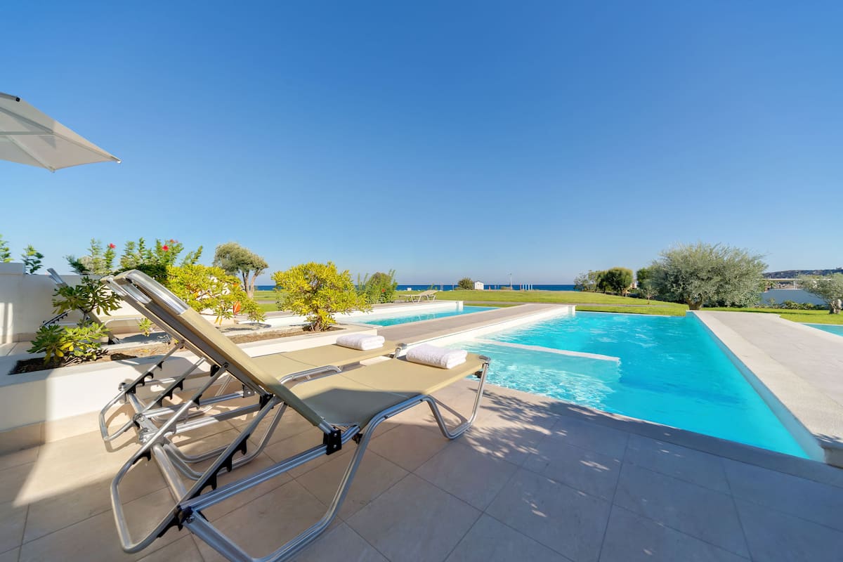 Uma área à beira da piscina com espreguiçadeiras e vista para o mar.