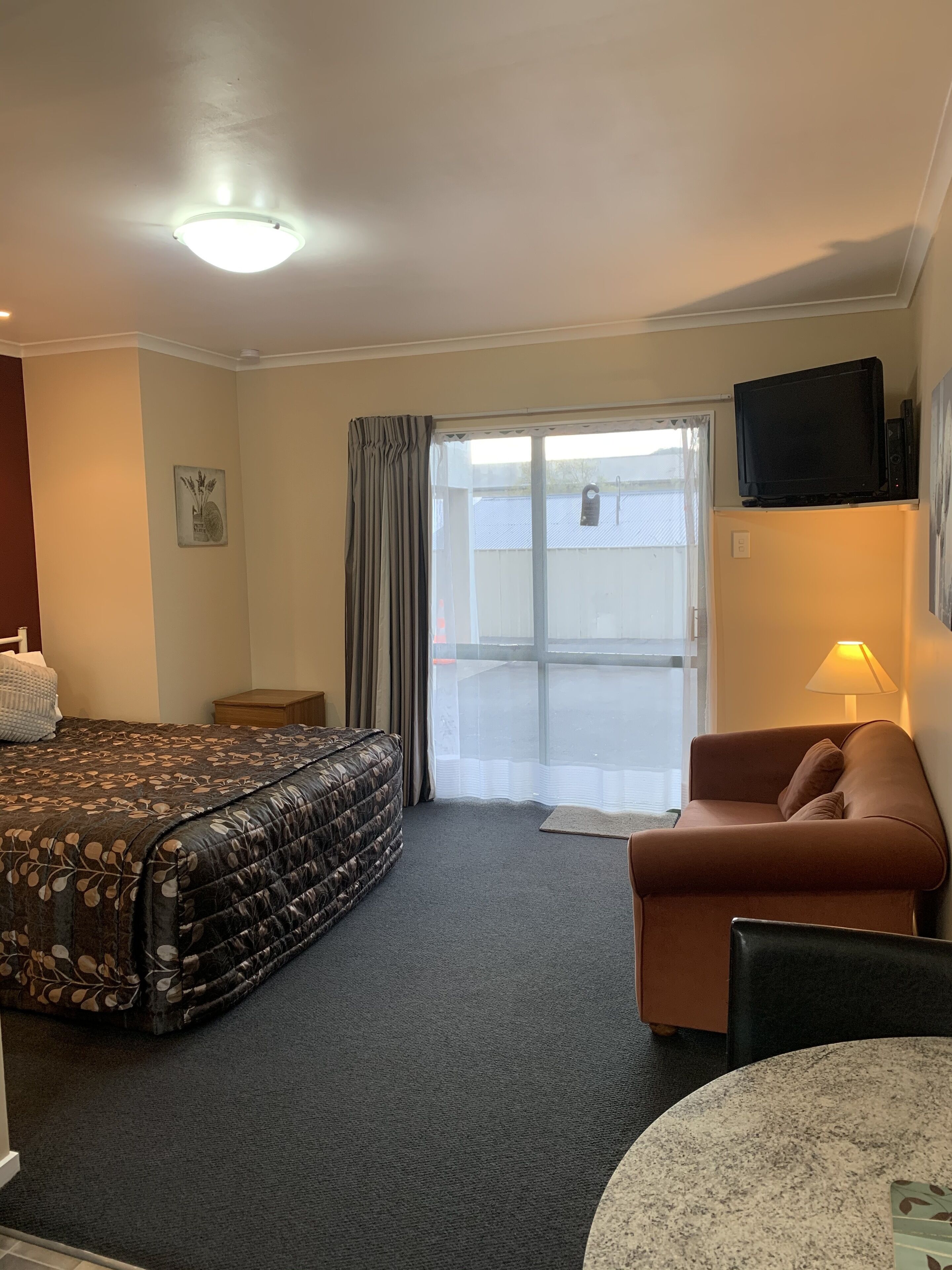 Quarto de hotel com uma cama, um sofá, uma televisão e uma porta de vidro deslizante para o exterior.