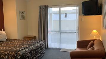 Quarto de hotel com uma cama, um sofá, uma televisão e uma porta de vidro deslizante para o exterior.