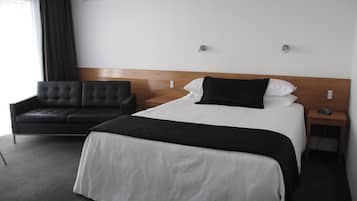 Quarto de hotel com uma cama, um sofá preto, cabeceira de madeira e mesa de cabeceira com um telefone.