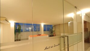Um hall de hotel com uma receção, um separador de vidro e vista para o exterior.