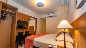 Quarto de hotel com cama, luminária de cabeceira, televisão e escrivaninha com cadeiras.