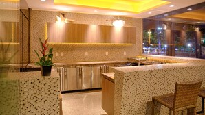 Cozinha moderna com área de bar, eletrodomésticos de aço inoxidável e vista para o exterior através de uma grande janela.