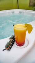 Um copo de sumo de laranja com uma fatia de limão sobre uma superfície branca, ao lado de um par de óculos de sol.