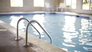 Piscina interior com escadas de metal e borda revestida de azulejos.