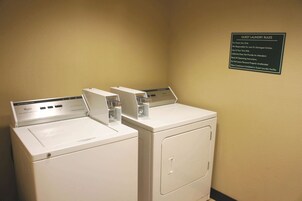 Uma lavanderia com duas máquinas de lavar e uma secadora, e uma placa com as regras para uso dos hóspedes.