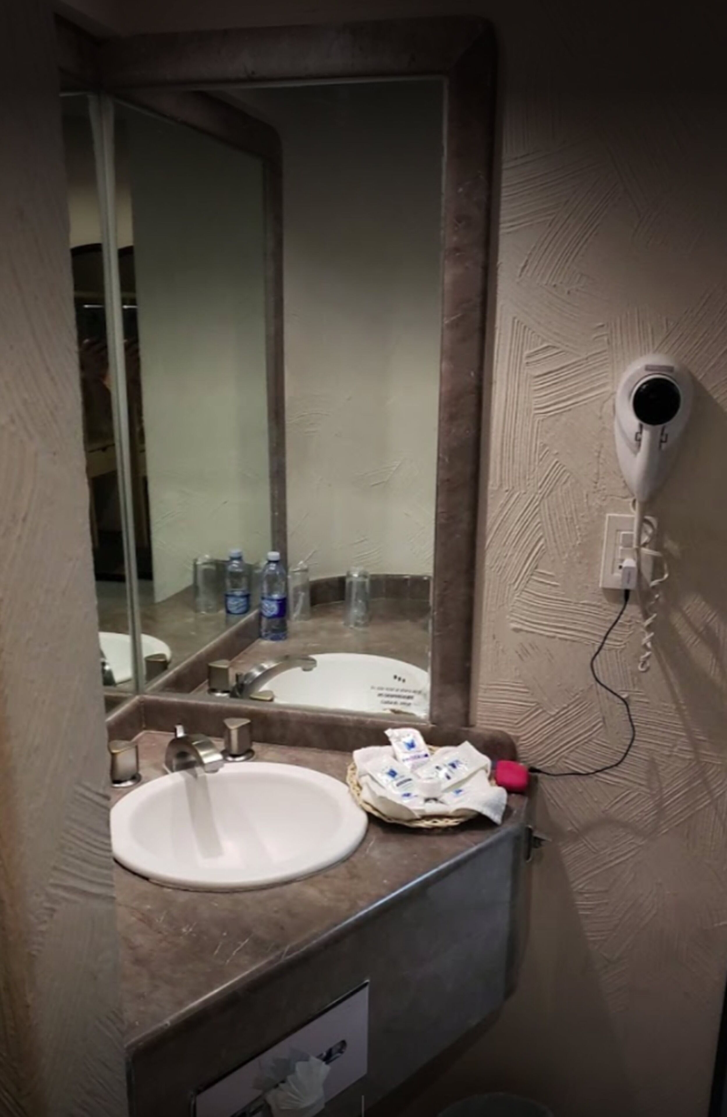 Casa de banho com um espelho grande, uma pia e um secador de cabelo fixado na parede.