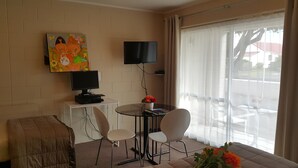 Um quarto com televisão, um quadro, mesa com cadeiras, sofá e janela com cortinas.